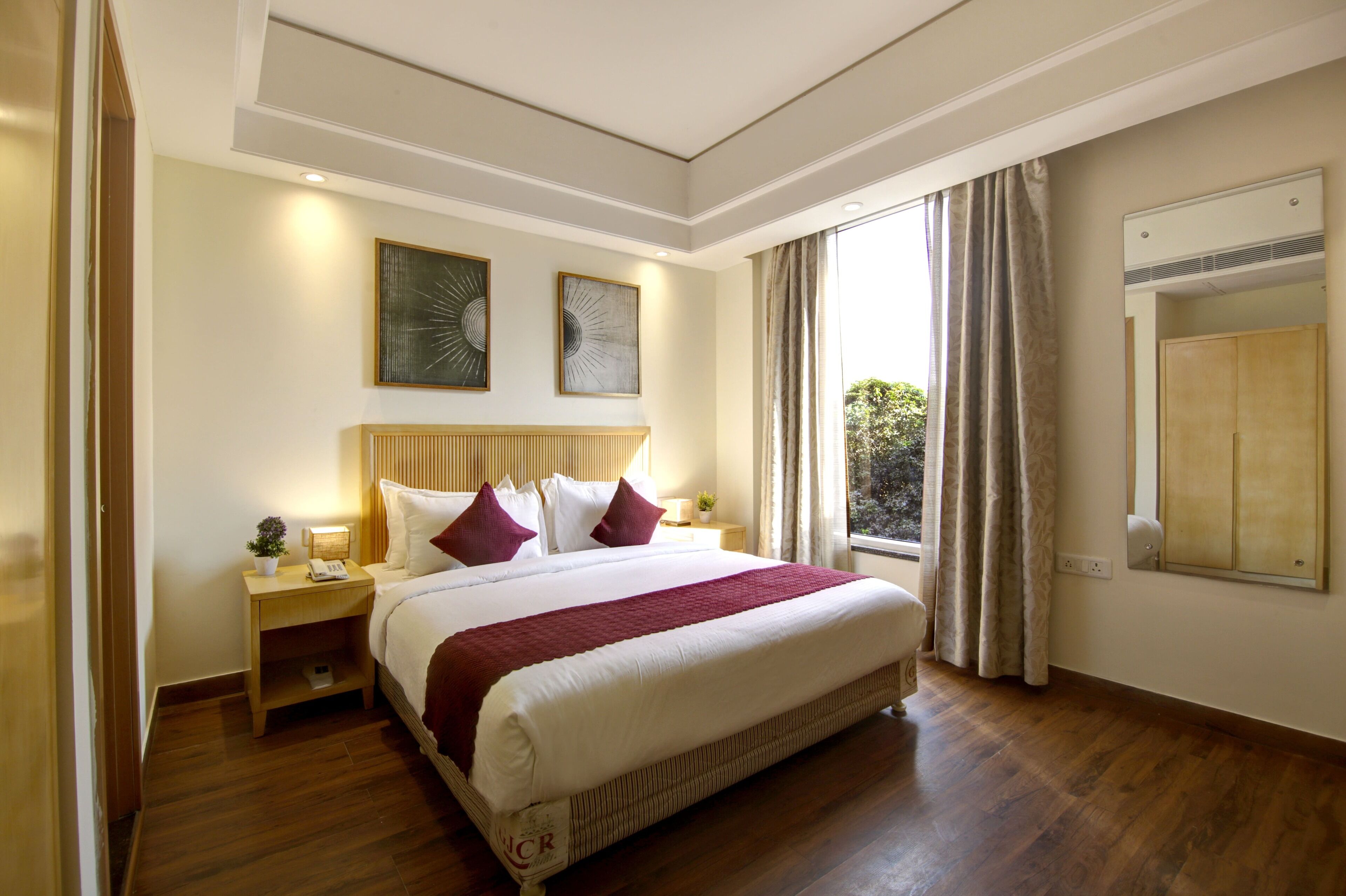 Quarto de hotel com uma cama grande, mesa de cabeceira e ar condicionado fixado na parede, além de cortinas na janela.