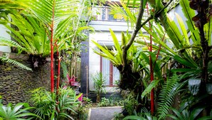 Um jardim exuberante com muro de pedra, um caminho e um edifício com varanda ao fundo.