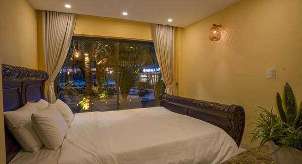 Quarto de hotel com uma cama grande, cortinas, vista para o exterior e um vaso de planta.