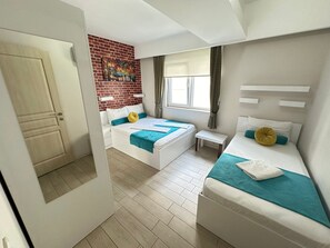 Quarto de hotel moderno com parede de tijolos decorativa, duas camas, uma mesinha e uma janela com cortinas.