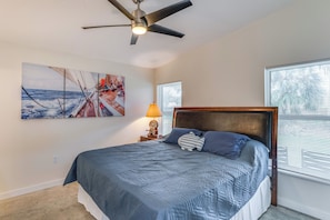 Um quarto com uma cama, um ventilador de teto, uma janela com persianas e um quadro na parede.