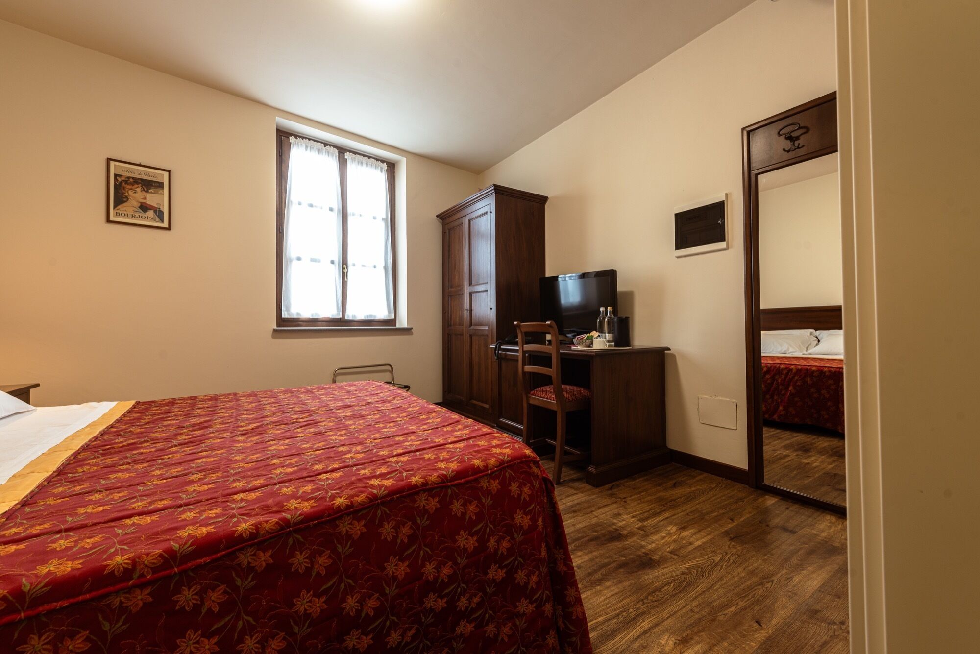 Quarto com cama, escrivaninha, televisão e guarda-roupa.