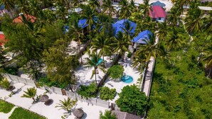 Vista aérea de um resort costeiro com várias construções em estilo bungalow, palmeiras e uma área de praia arenosa com piscina.