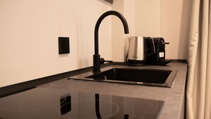 Uma cozinha moderna com uma torneira preta, uma cafeteira de aço inoxidável e uma bancada preta.