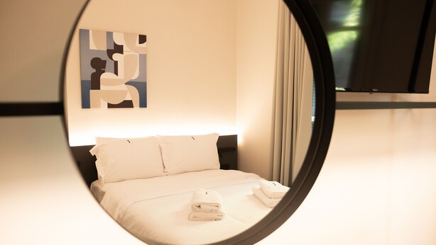 Quarto de hotel moderno com cama, espelho redondo e televisão de tela plana.