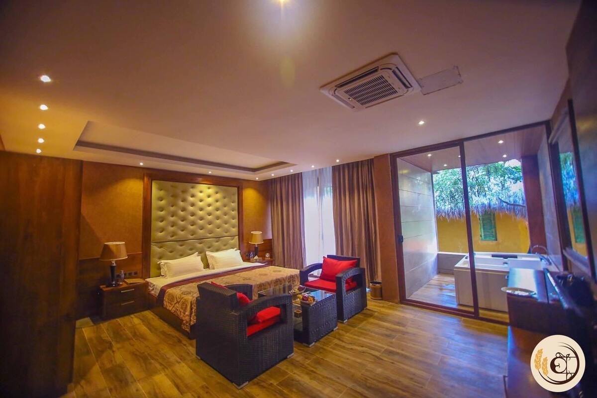 Quarto de hotel moderno com uma cama grande, área de estar separada, banheiro com banheira e uma janela ampla com vista para o exterior.