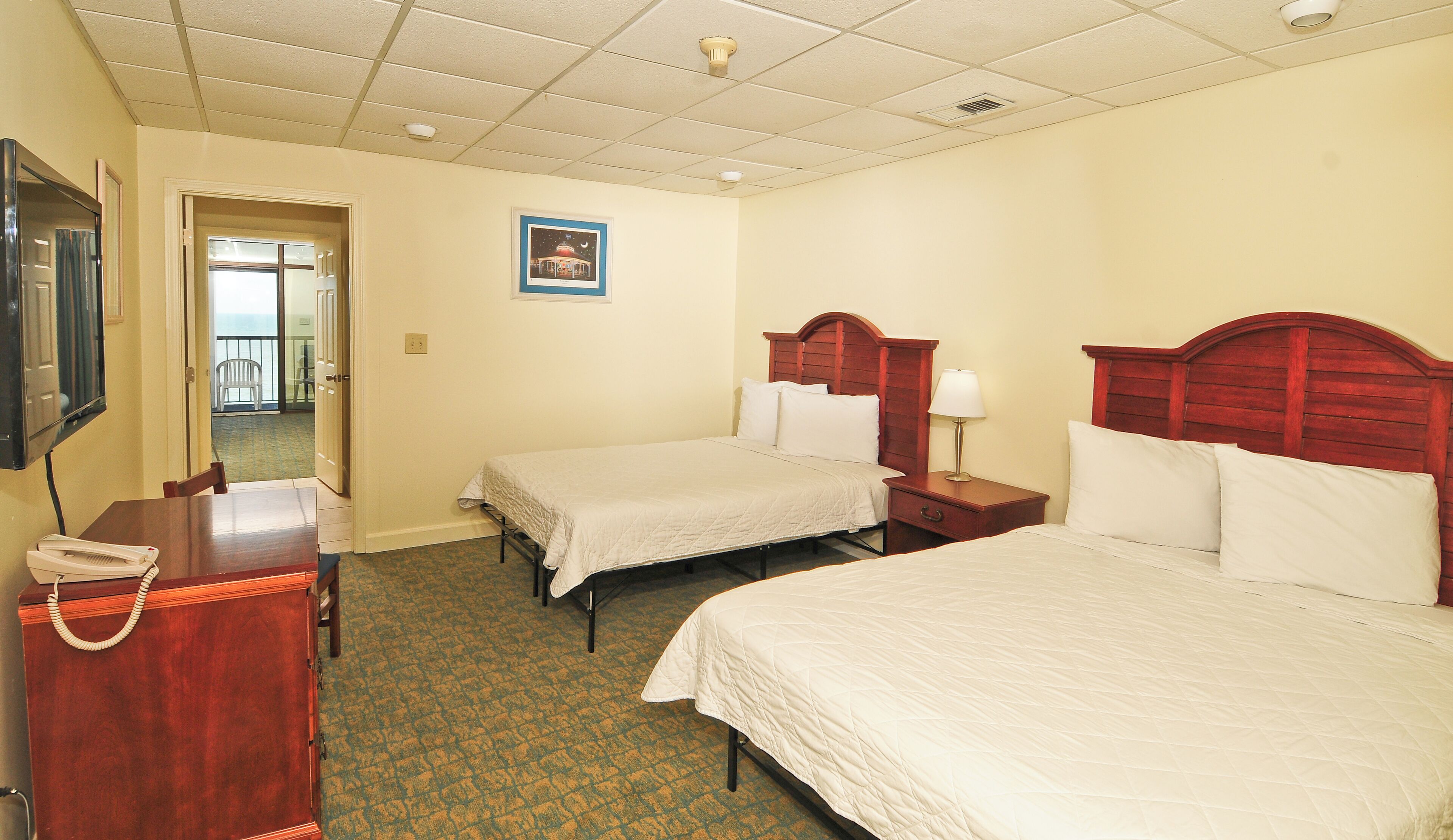 Quarto de hotel com duas camas, uma escrivaninha, uma cadeira e uma televisão.