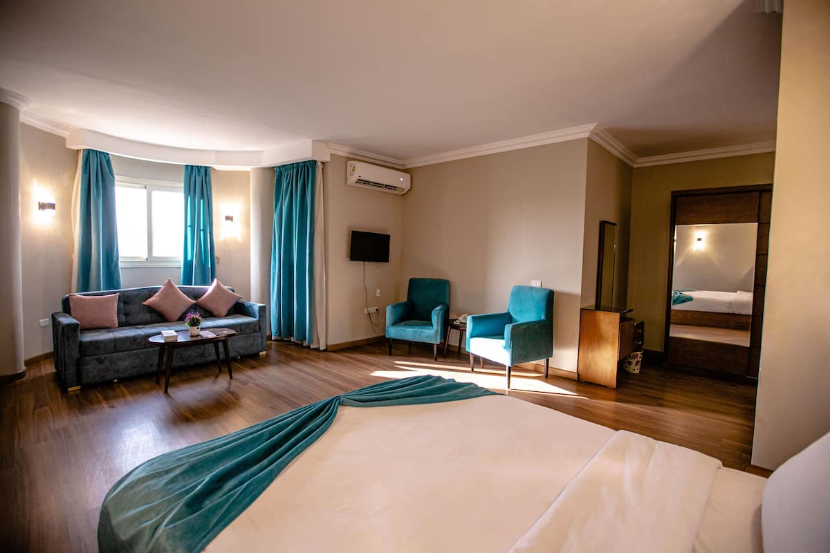Quarto de hotel com cama, sofá, duas poltronas, uma mesinha e televisão.