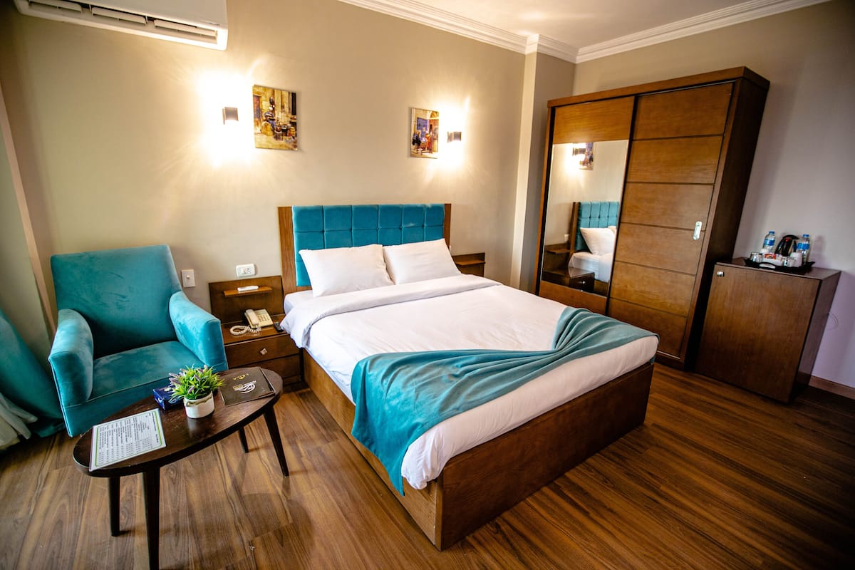 Quarto de hotel com cama, cadeira, escrivaninha e guarda-roupa.