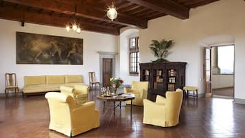 Um quarto espaçoso com uma grande pintura, um sofá, poltronas amarelas, uma mesa de centro de madeira e uma estante de livros.
