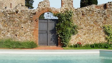 Um edifício de pedra com portão de metal, piscina e vegetação.