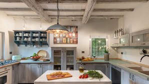 Cozinha com ilha central, armários de madeira, luminária pendente e janela com vista.