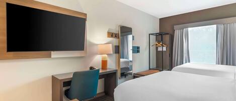Quarto de hotel com cama, escrivaninha, cadeira, televisão e janela com cortinas.