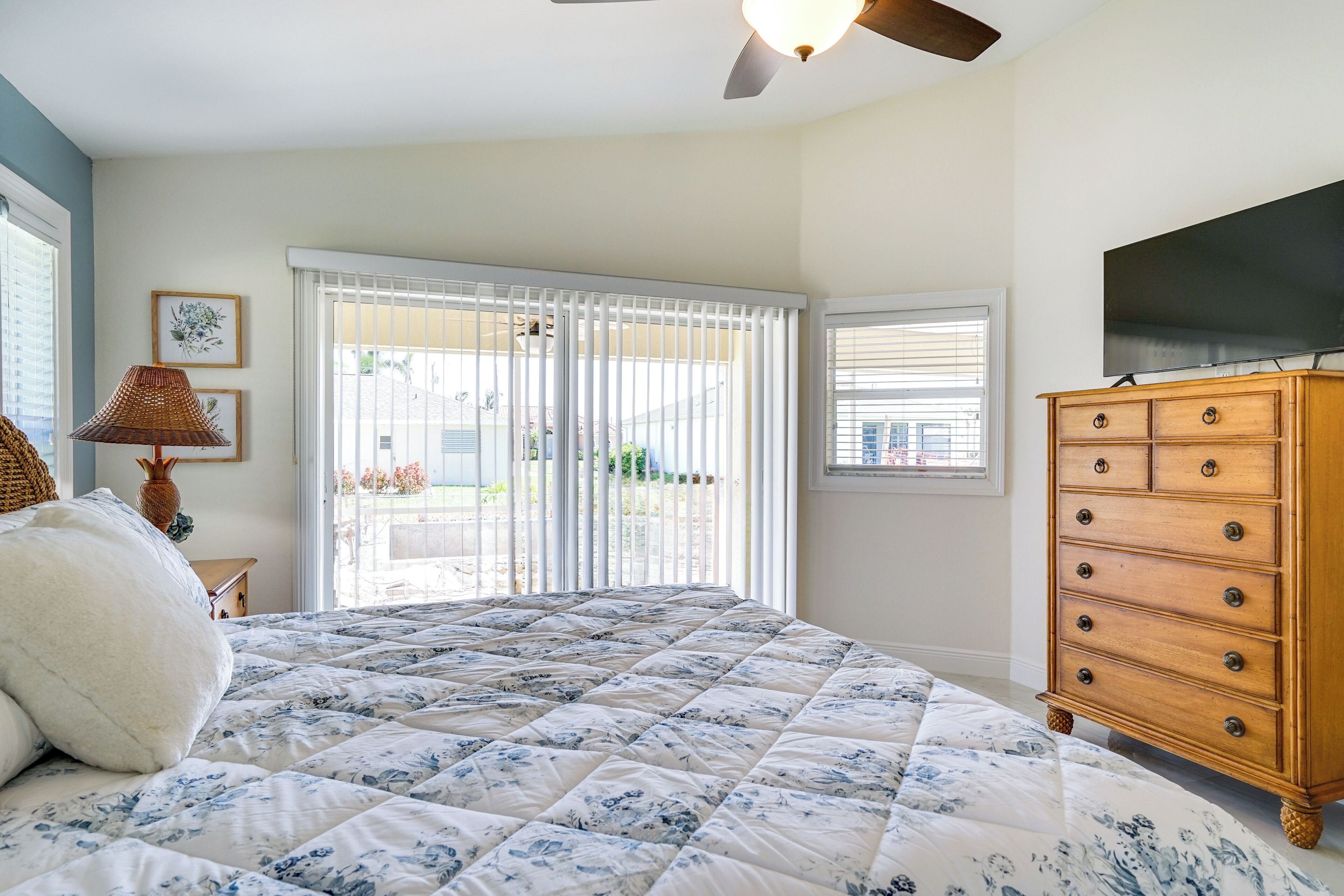 Quarto com cama, cômoda, ventilador de teto e janela com persianas.