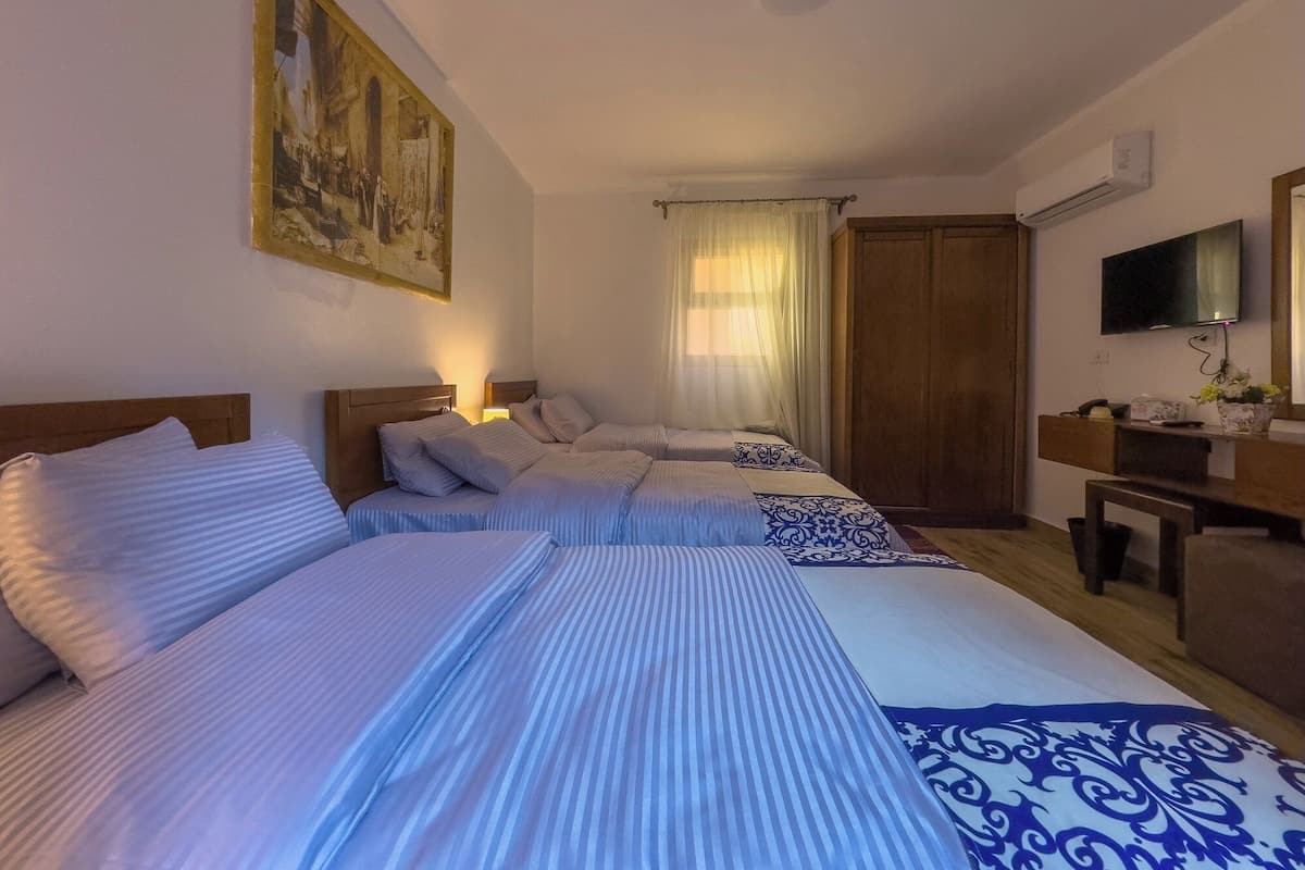 Quarto de hotel com três camas, um guarda-roupa de madeira, uma televisão e um quadro na parede.