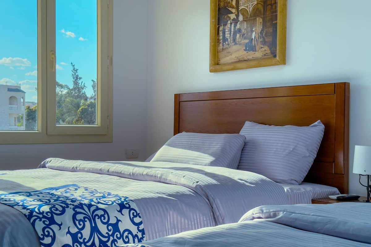 Quarto com uma grande janela, cabeceira de madeira e um quadro na parede.