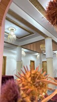 Quarto com teto alto, vigas de madeira e paredes brancas. Há colunas que sustentam o teto, e um candelabro pendurado nele.