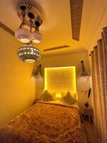 Quarto com colcha estampada, cabeceira decorativa e várias luminárias pendentes.