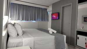 Quarto pequeno e bem organizado, com uma cama, televisão e frigorífico.