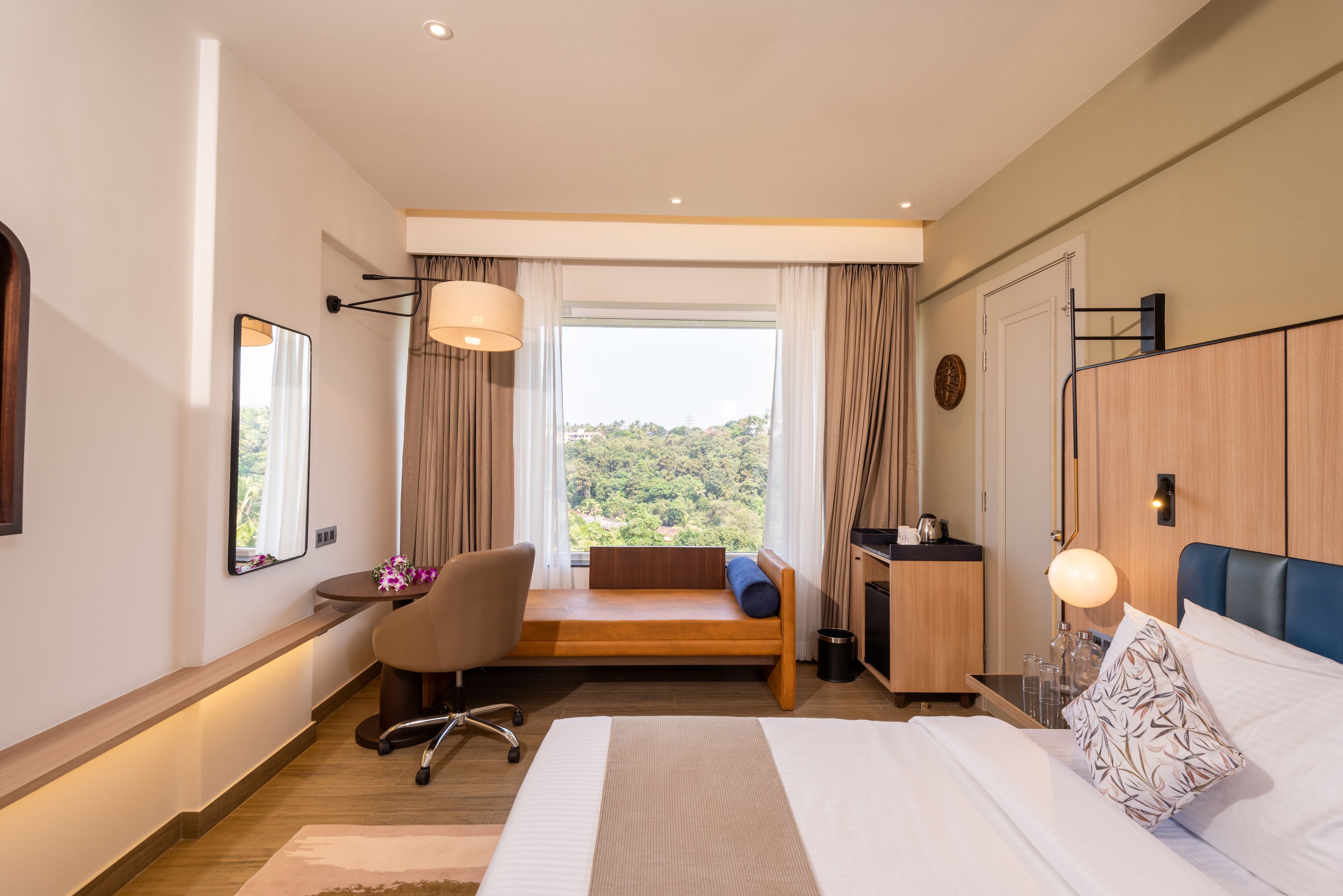 Quarto de hotel moderno com cama, escrivaninha, cadeira e vista para o exterior.