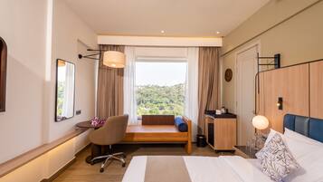 Quarto de hotel moderno com cama, escrivaninha, cadeira e vista para o exterior.