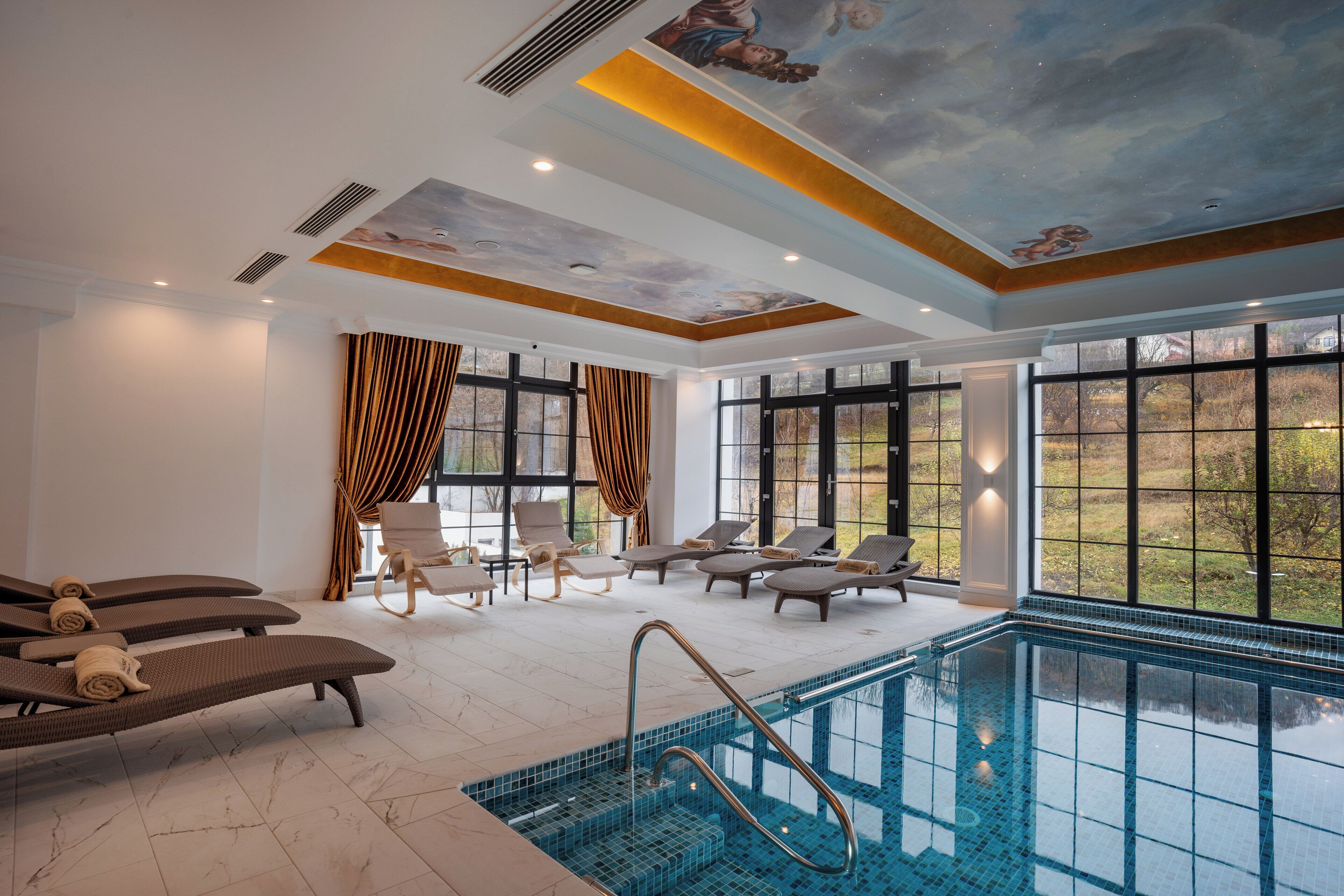 Uma área de piscina interior ampla, com espreguiçadeiras e um mural no teto.
