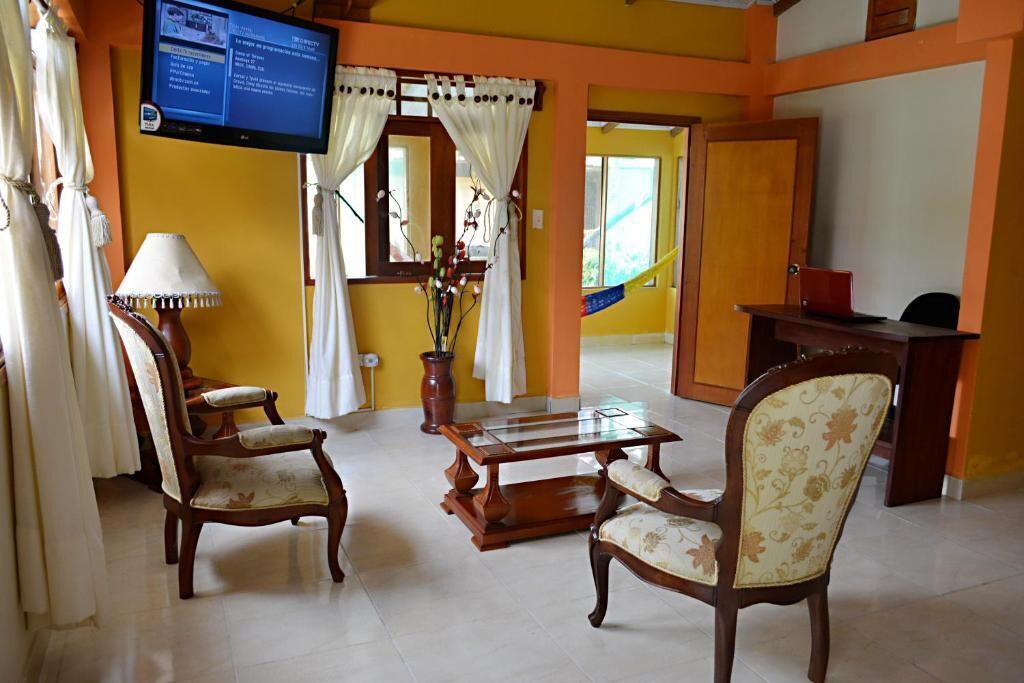 Quarto com uma mesa de madeira, duas cadeiras, uma TV na parede e uma porta que dá para outro cômodo.
