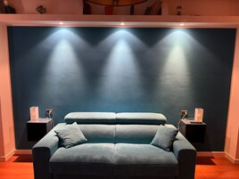 Uma sala de estar moderna com parede azul escura, sofá azul claro e duas mesinhas de cabeceira com luminárias.