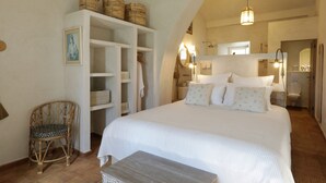Quarto com cama grande, guarda-roupa branco, cestos de vime, cadeira de vime e um banco de madeira.