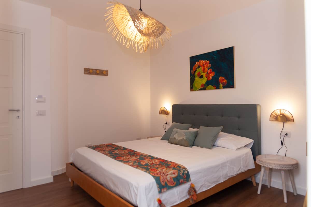 Quarto com cama, quadro na parede, luminária pendente e mesa de cabeceira.