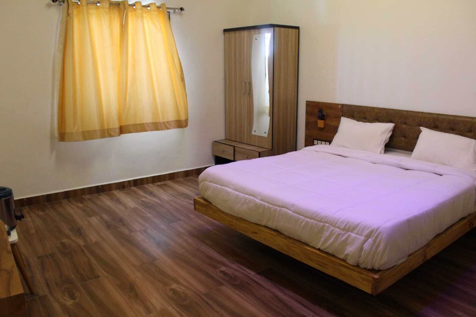 Quarto com cama de madeira, guarda-roupa, mesa de cabeceira e cortina.