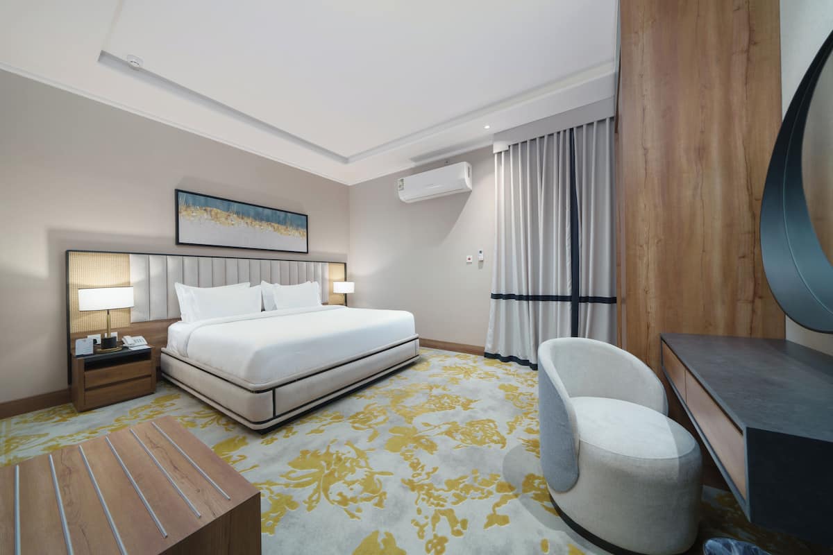 Quarto de hotel com cama, escrivaninha, cadeira, mesa de cabeceira e ar condicionado.