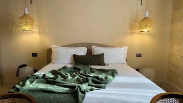 Cama bem arrumada com travesseiros brancos e verdes, manta verde e duas luminárias fixadas na parede.