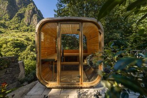 Uma cabana de madeira com porta de vidro, cercada por vegetação exuberante e uma paisagem montanhosa.