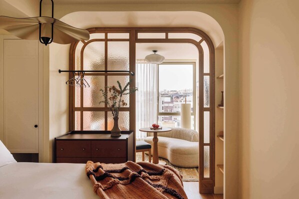 Quarto de hotel com uma cama, penteadeira, janela com vista para a cidade, mesinha com um vaso e uma cadeira.