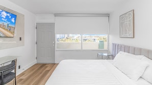Quarto moderno com cama grande, escrivaninha e janela com vista para a cidade.