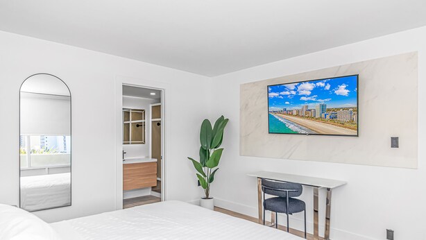 Quarto de hotel moderno com cama, escrivaninha, cadeira, janela ampla e pintura com vista urbana.