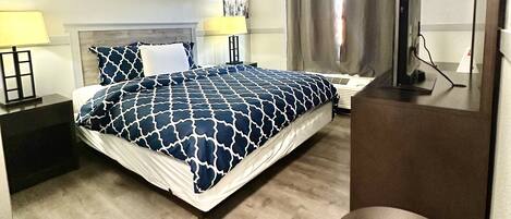 Quarto de hotel com cama, escrivaninha, cadeira, televisão e abajur.
