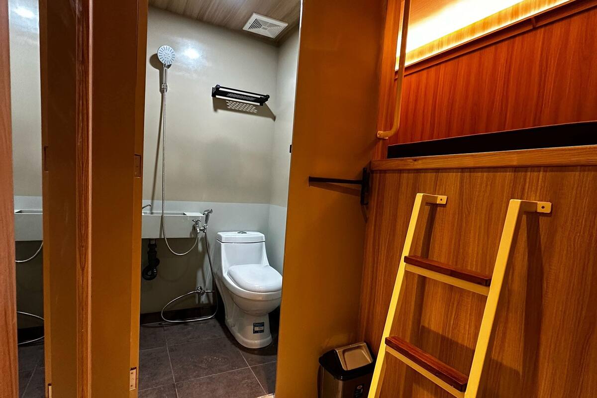 Casa de banho compacta com sanita, chuveiro e escada de madeira.