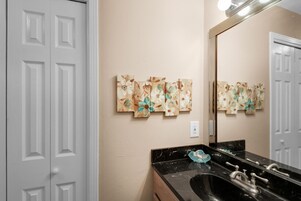 Uma casa de banho com lavatório em mármore preto, um espelho e arte floral na parede.
