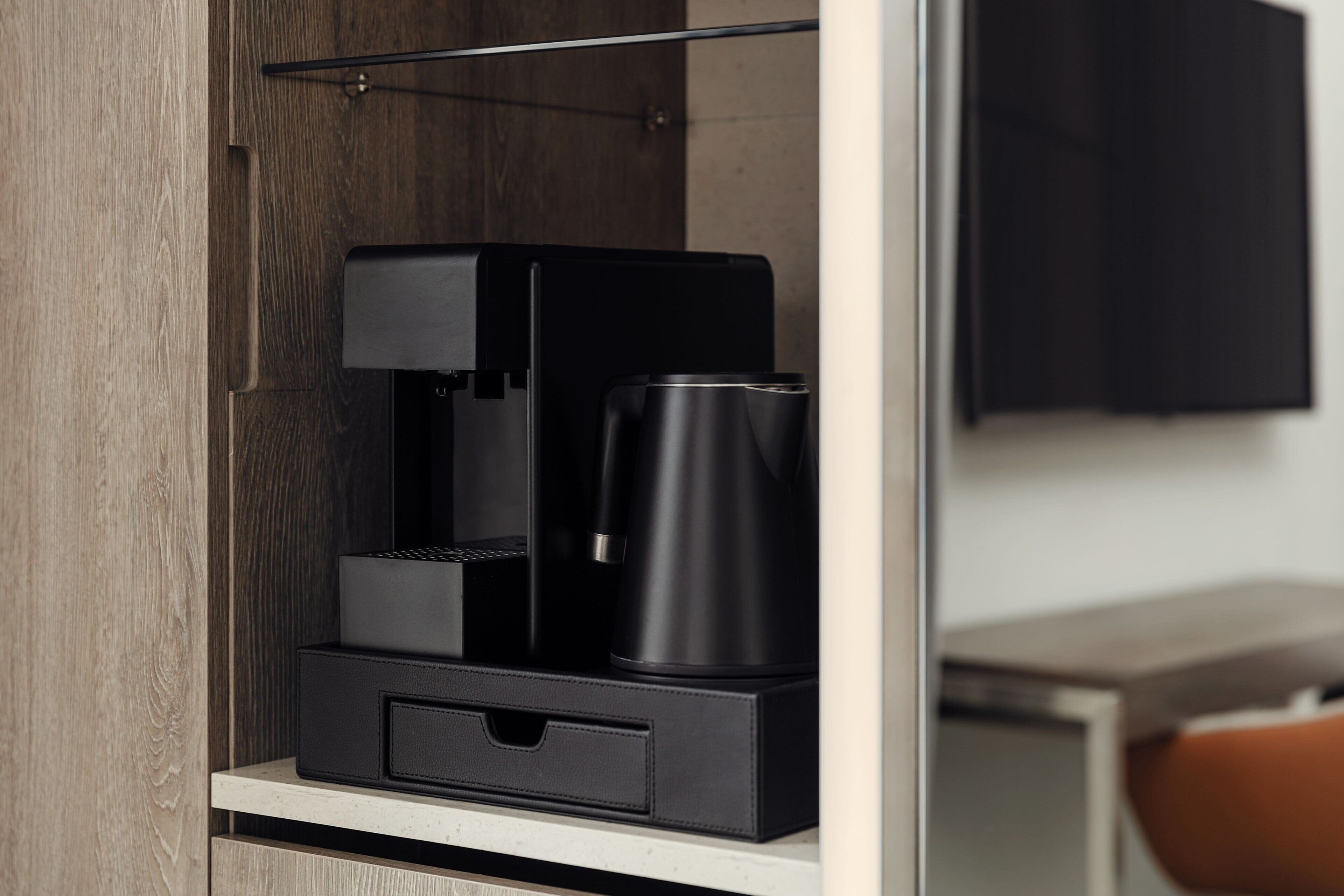 Uma máquina de café e uma chávena numa estante, num quarto com painéis de madeira e televisão na parede.