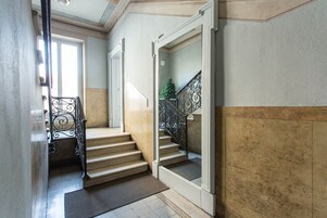 Uma escadaria com corrimão de metal, um tapete na entrada e uma porta que dá para outro cômodo.