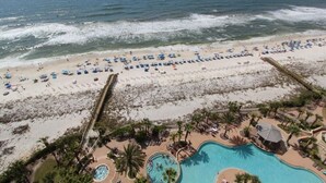Vista aérea de um resort à beira-mar, com uma grande piscina, guarda-sóis e palmeiras.