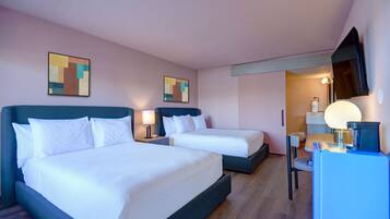 Quarto de hotel com duas camas, uma escrivaninha, uma cadeira e obras de arte nas paredes.