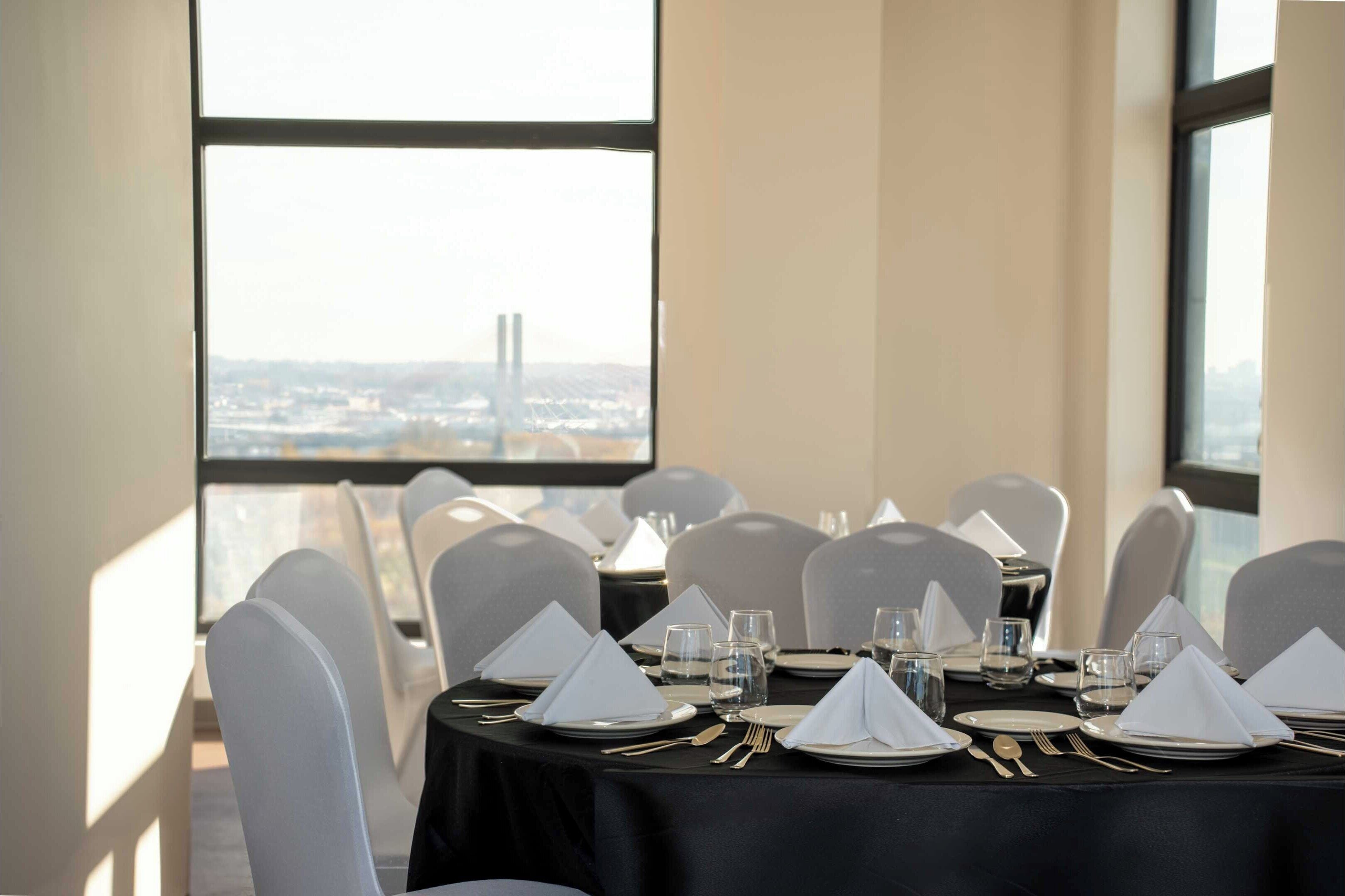 Uma sala de conferências com uma mesa posta para uma reunião, cadeiras dispostas ao redor e uma grande janela com vista para a cidade.