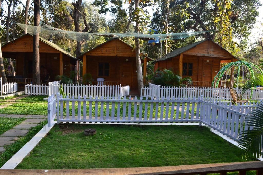Uma fileira de cabanas de madeira com cercas brancas de piquete, rodeadas por árvores e grama.