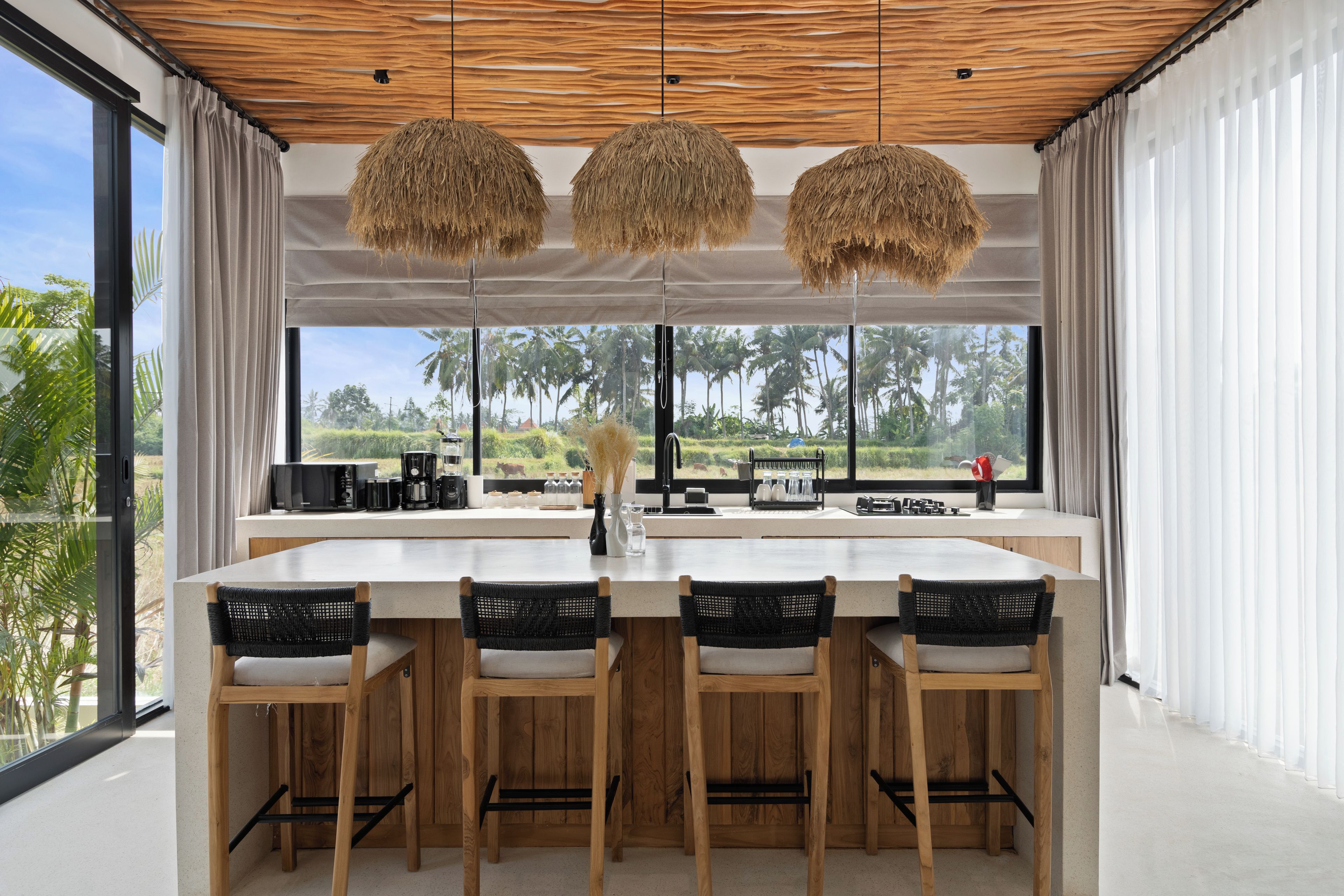 Cozinha moderna com uma ilha grande, banquetas e vista para palmeiras.