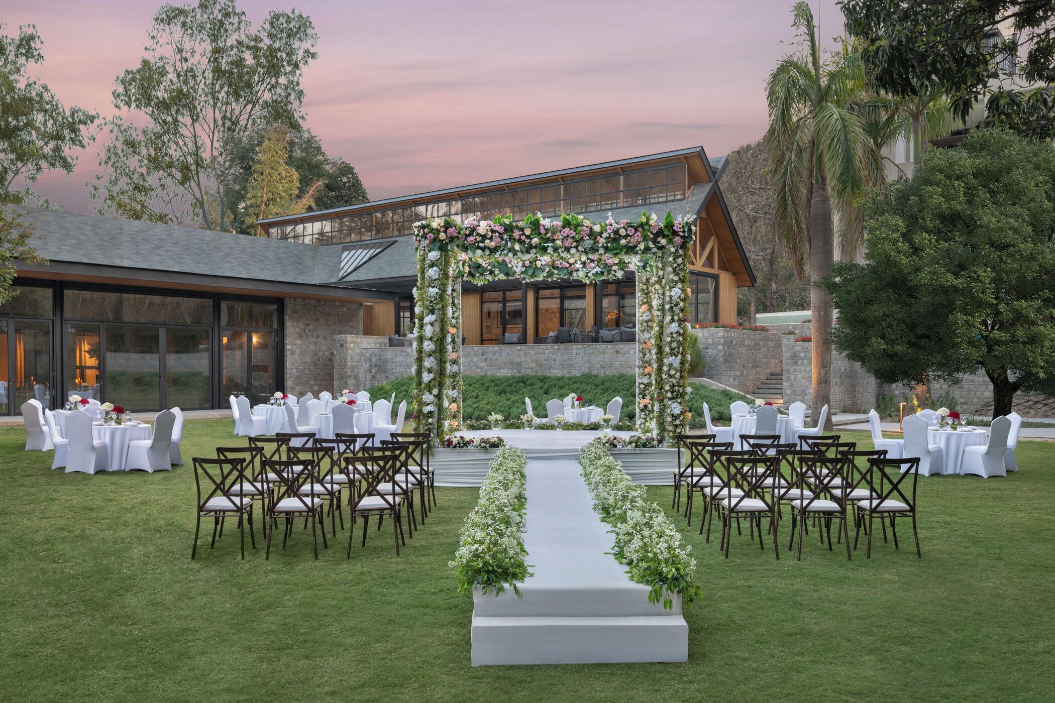 Espaço para casamento ao ar livre, com arco branco, mesas e cadeiras dispostas para os convidados.