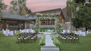 Espaço para casamento ao ar livre, com arco branco, mesas e cadeiras dispostas para os convidados.