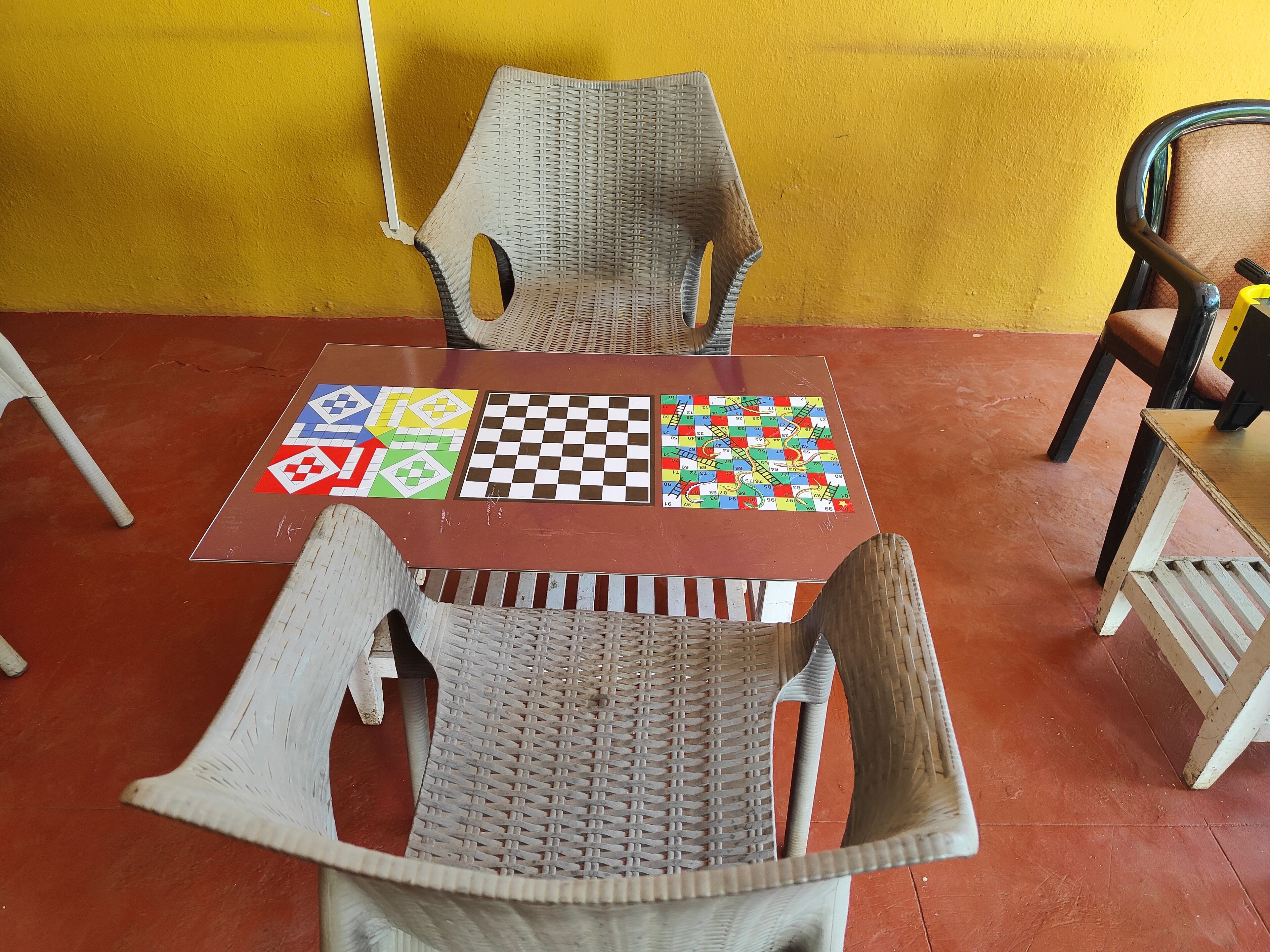Uma mesa com tabuleiro xadrez e azulejos coloridos, rodeada por cadeiras de vime.